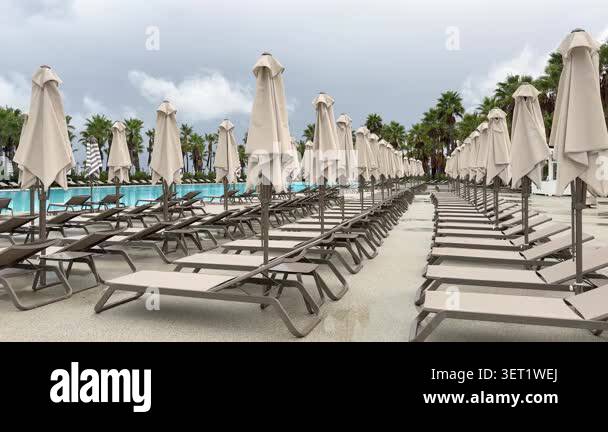 Sun loungers and closed umbrellas by resort pool on cloudy day Stock ...