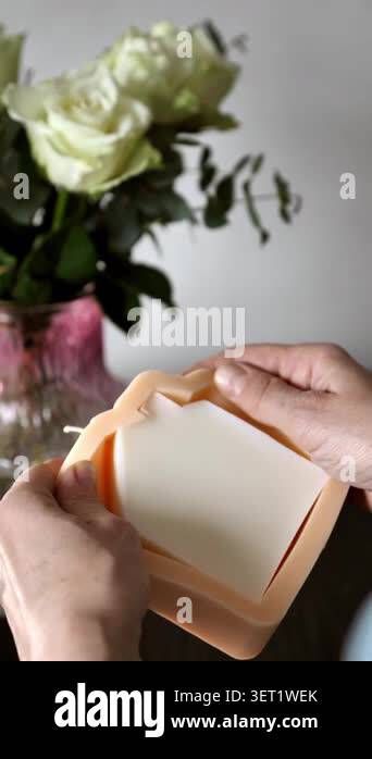 Hands removing a white house-shaped soy candle from a flexible silicone ...