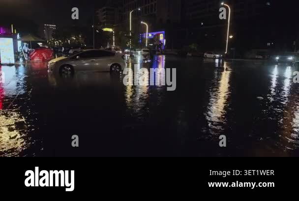 Cars and motorbikes navigate a flooded city intersection during heavy ...