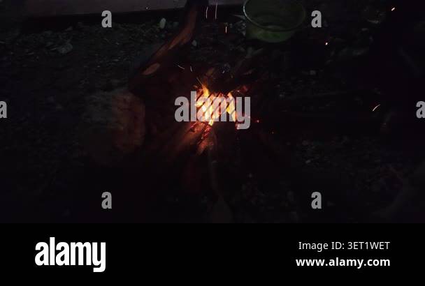 Close up: a person turns two fish grilling over crackling flames and ...