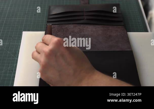 Artisans hands punching holes in a dark leather wallet with a special ...