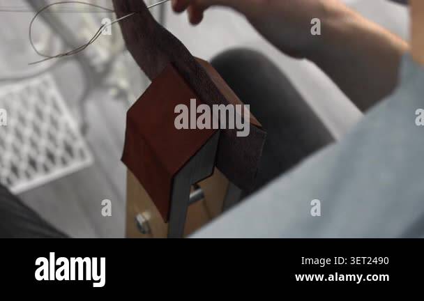 Detailed view of a craftsmans hands carefully saddle stitching a brown ...