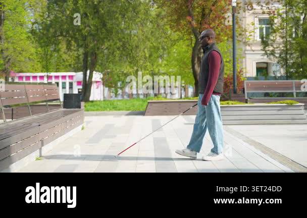 Confident blind man walking in a city park with a white cane, finding a ...