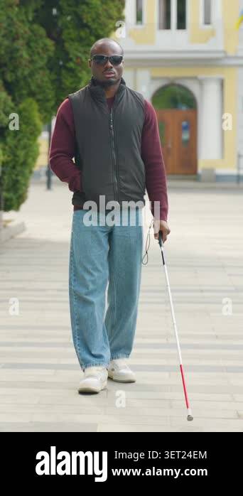 Independent man with blindness navigating a city sidewalk using a white ...