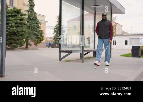 Young black man with blindness using a long white cane to navigate the ...