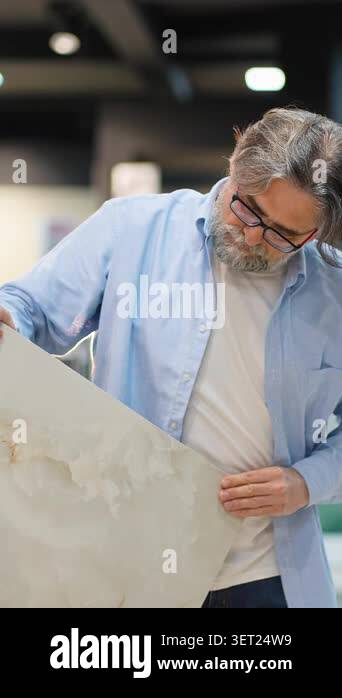 Older man with glasses and a beard carefully selecting large ceramic ...