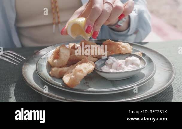 Female hands squeezing fresh lemon juice on a plate of crispy fried ...