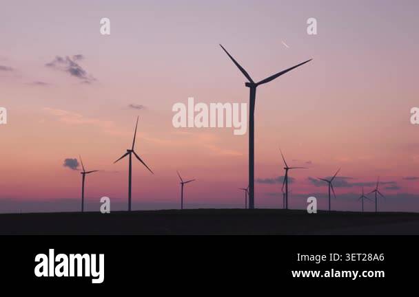 Silhouettes of wind turbines spinning in a field against a colorful ...