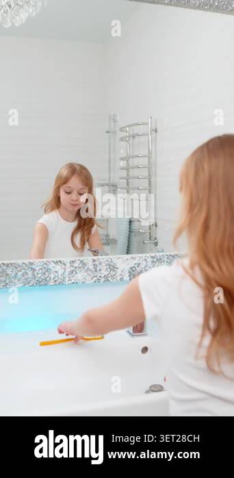 Young girl standing alone in bathroom brushing her teeth in front of ...