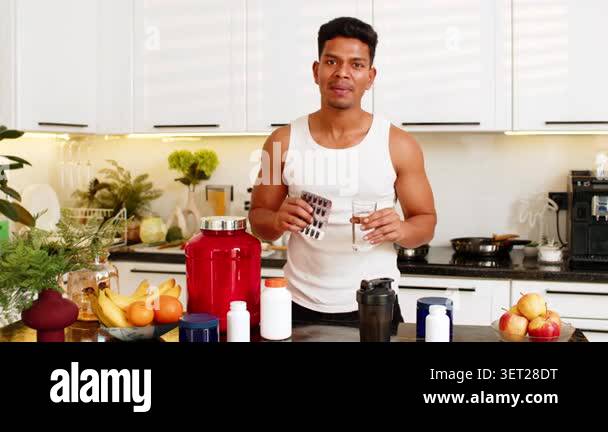 Indian man showing sports supplements and water in home kitchen while ...