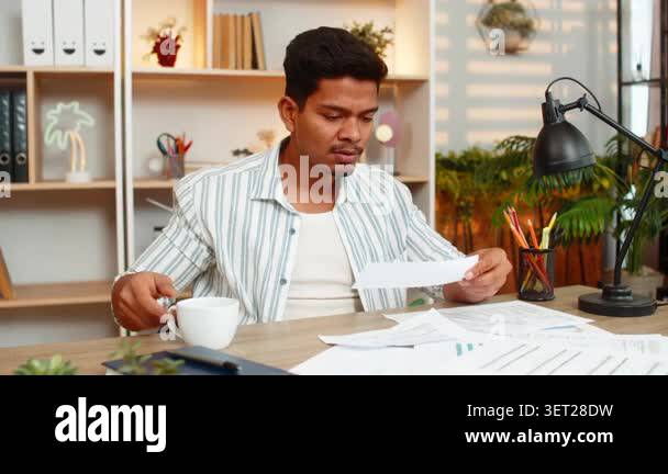 Indian man on home table drinks coffee and reads documents during ...