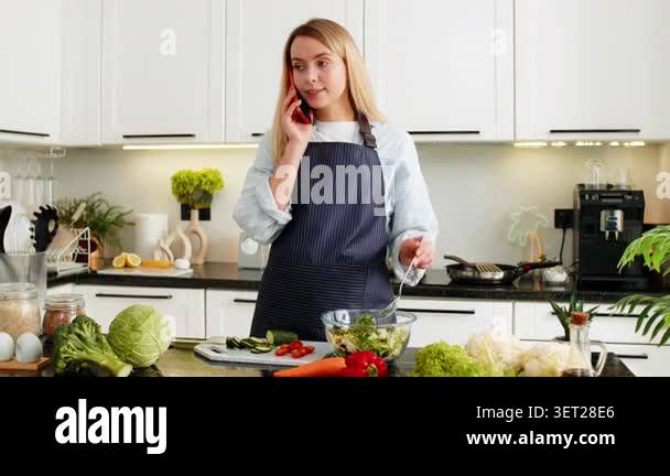 Middle-aged woman talks on smartphone while mixing vegetable salad for ...