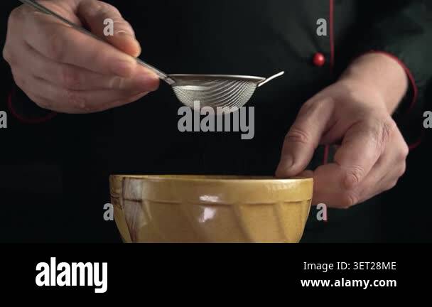 Chef in a black uniform carefully sifts cocoa powder through a fine ...