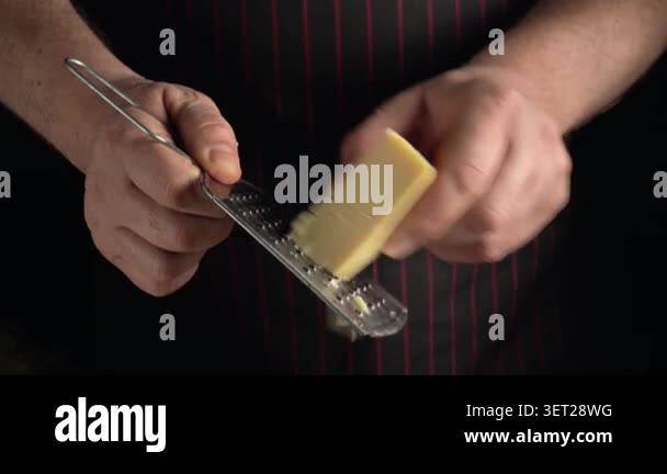 Hands actively grating a block of cheese using a stainless steel grater ...
