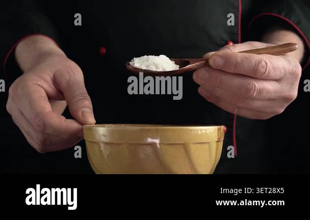 Chef hands in black attire pour granulated sugar from a wooden spoon ...