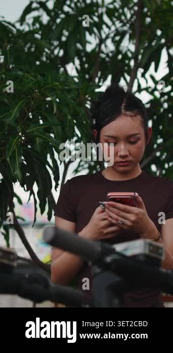 Stylish asian woman scrolling on her mobile phone while standing next ...