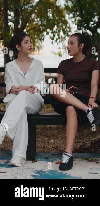Two young Asian girls enjoying a friendly conversation sitting on a ...