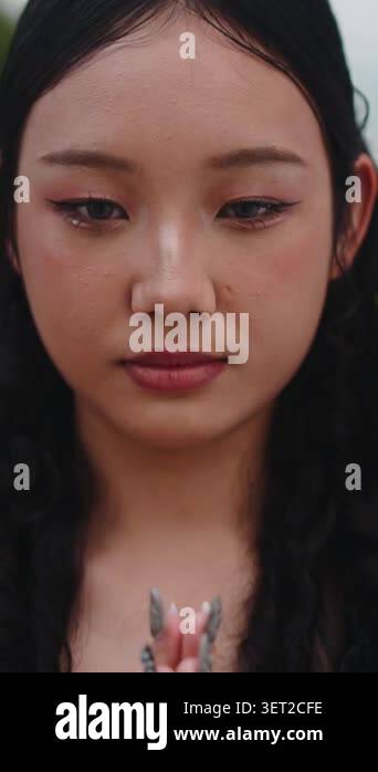 Spiritual young asian woman with long curly hair praying outdoors ...