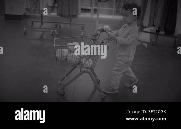 A young toddler in light pajamas and sneakers pushes a small metal ...
