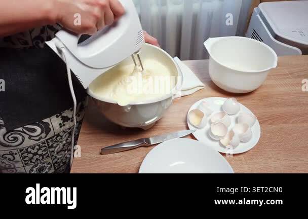 A person is actively mixing a light-colored batter or cream with a ...
