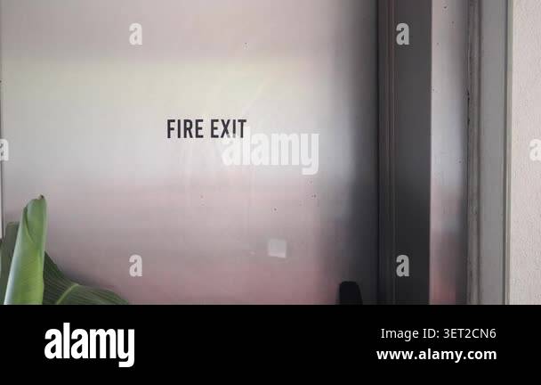 A sign marks the fire exit door at a busy building. People pass by ...