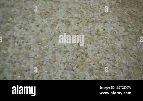 Close up of clear water flowing over pebbles and sand on a riverbed ...