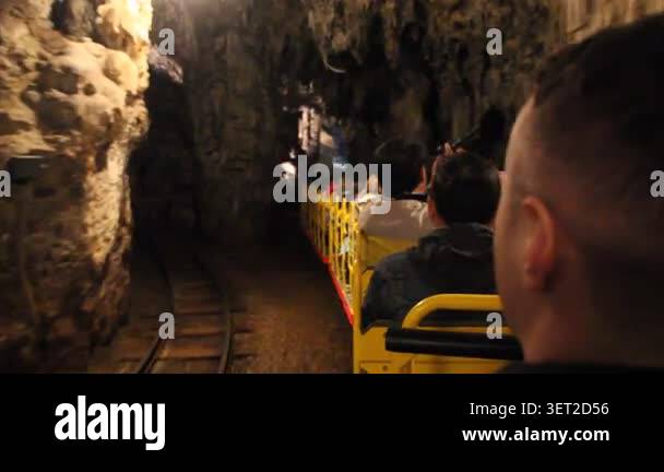 People riding yellow train through illuminated cave with stalactites ...