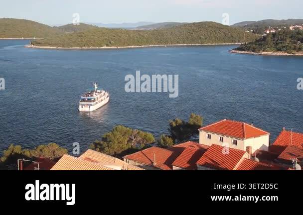 Wide shot of a passenger boat sailing on a calm blue sea near a green ...