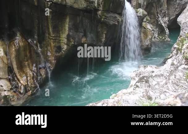 Turquoise water flows through a rocky gorge with a waterfall cascading ...