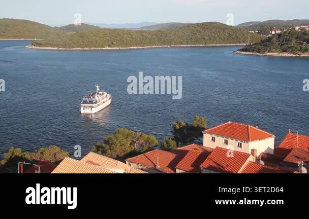Wide shot of a passenger boat sailing on a calm blue sea with green ...