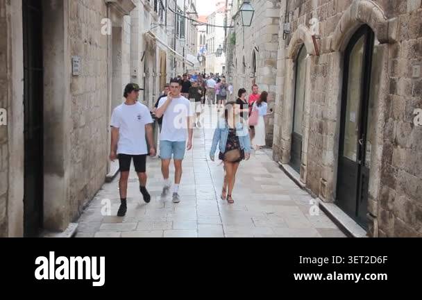 People walking down narrow stone street in old town, a small cat ...