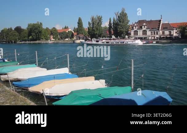 Boats covered with tarps are docked along a river with a passenger ship ...