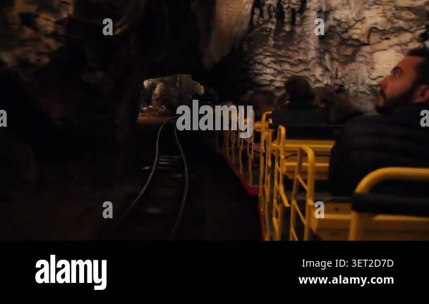 People riding yellow train through illuminated cave with stalactites ...