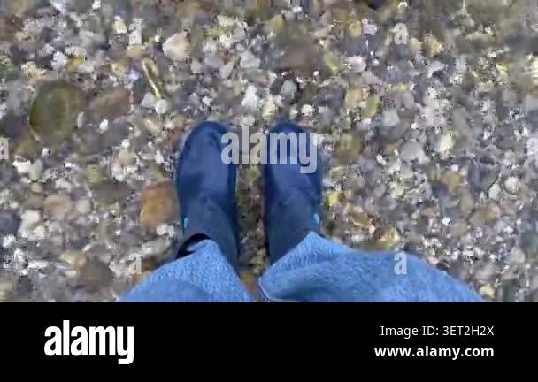 First-person view of feet in rubber boots standing in a clear rocky ...