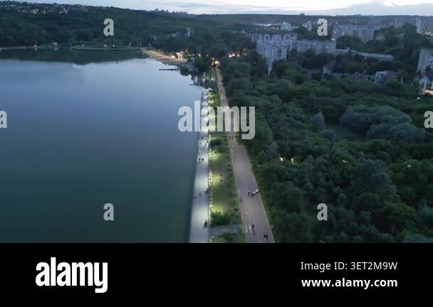 Drone footage following a lakeside promenade at dusk where small ...