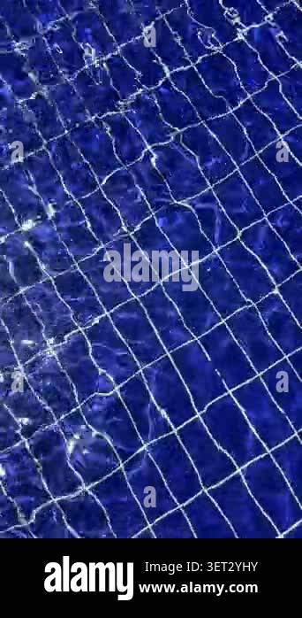 Sunlight reflecting on deep blue swimming pool tiles under clear water ...