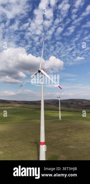 An aerial view of wind turbines standing in green fields under a blue ...