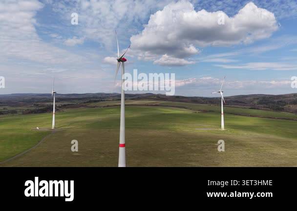 An aerial view of wind turbines standing in green fields under a blue ...