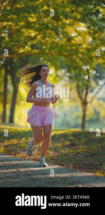 Athletic woman jogging on a path in a park during a sunny day, focusing ...