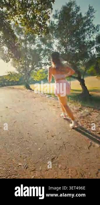 Back view of a young athletic woman jogging outdoors in a park during a ...