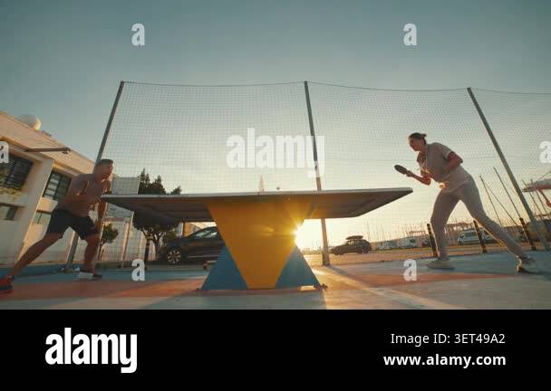Two individuals engage in a table tennis match at an outdoor area as ...