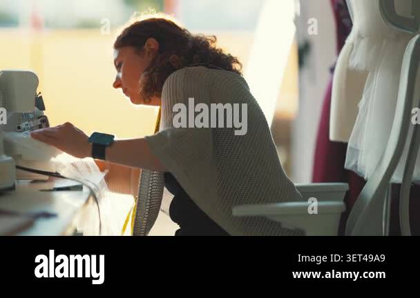 A person focuses on sewing fabric at a machine in a design studio. The ...