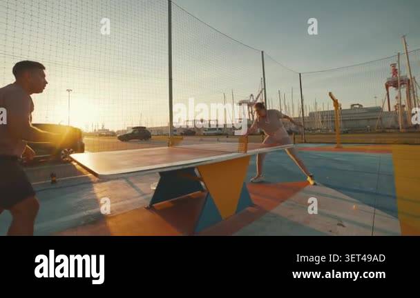 Two individuals engage in a game of table tennis at a waterfront ...