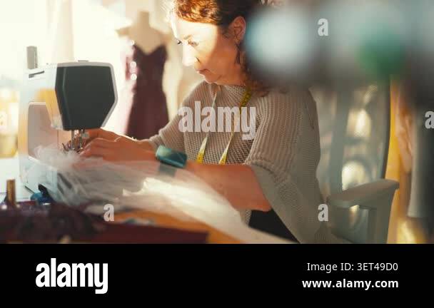 A seamstress focuses on sewing a dress in her workshop. She uses a ...