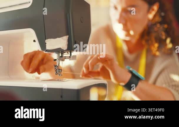 A person sews fabric using a sewing machine in a well-lit room. They ...