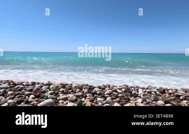 Wide scenic view of turquoise sea waves washing pebble beach under ...