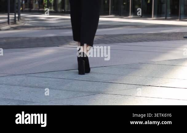 A person walks toward a modern building wearing black pants and shoes ...