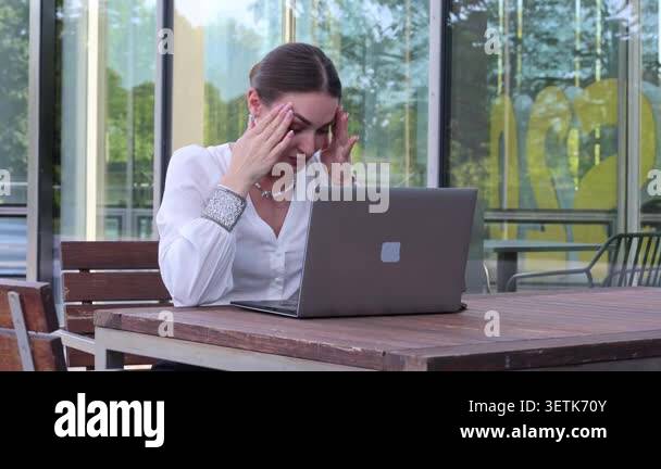 Woman sits at a table outside. She speaks into her computer. Her hands ...
