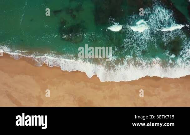 Aerial drone shot of turquoise ocean waves rolling onto sandy beach ...