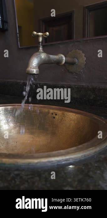 Close-up of an antique copper faucet pouring water into a traditional ...
